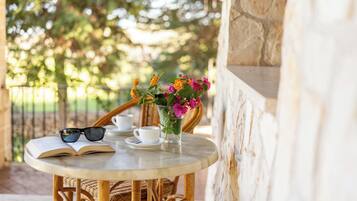 Uma mesa redonda com um livro, óculos de sol, um copo de água e um vaso com flores.