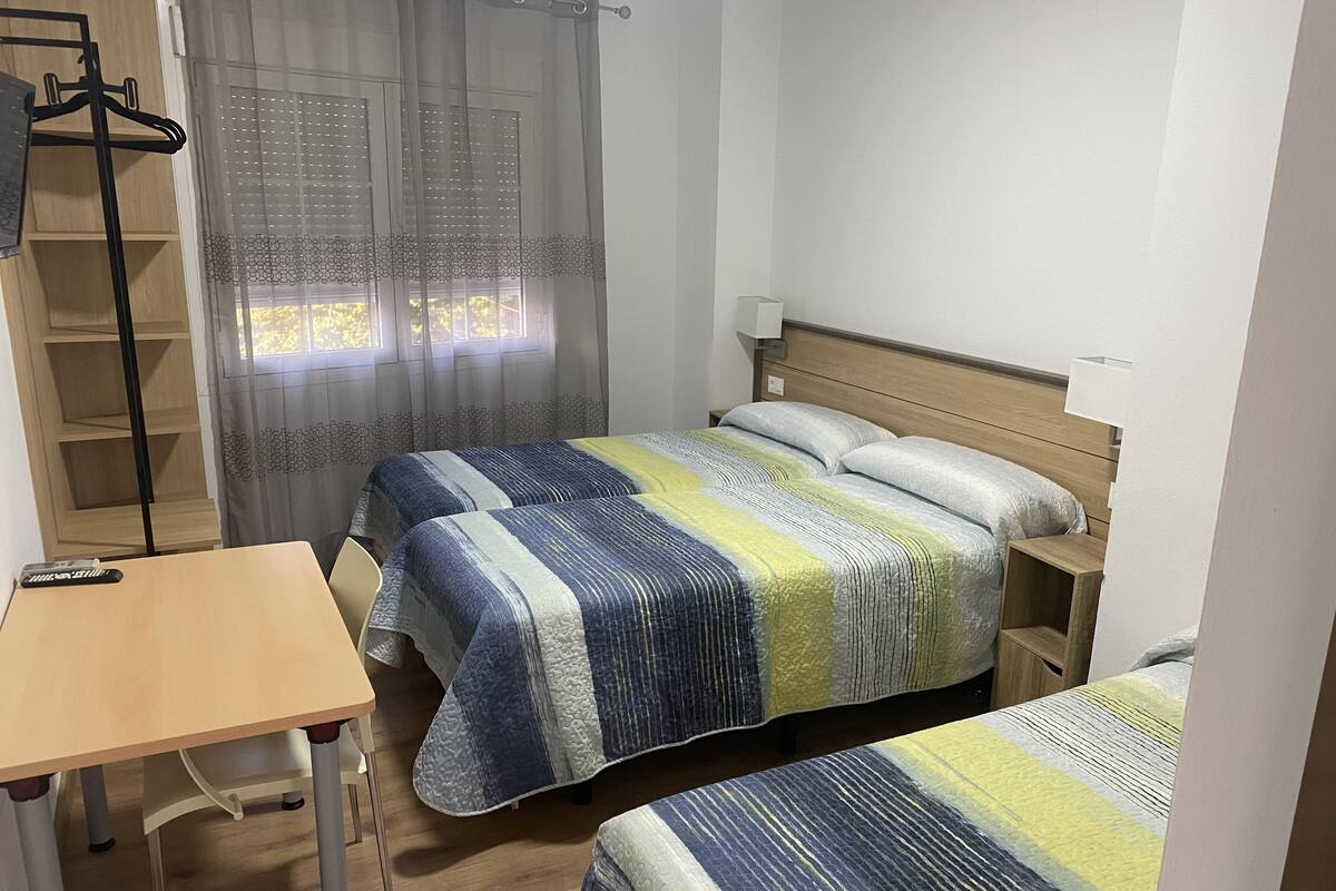 Quarto de hotel com duas camas, uma escrivaninha e uma cadeira.