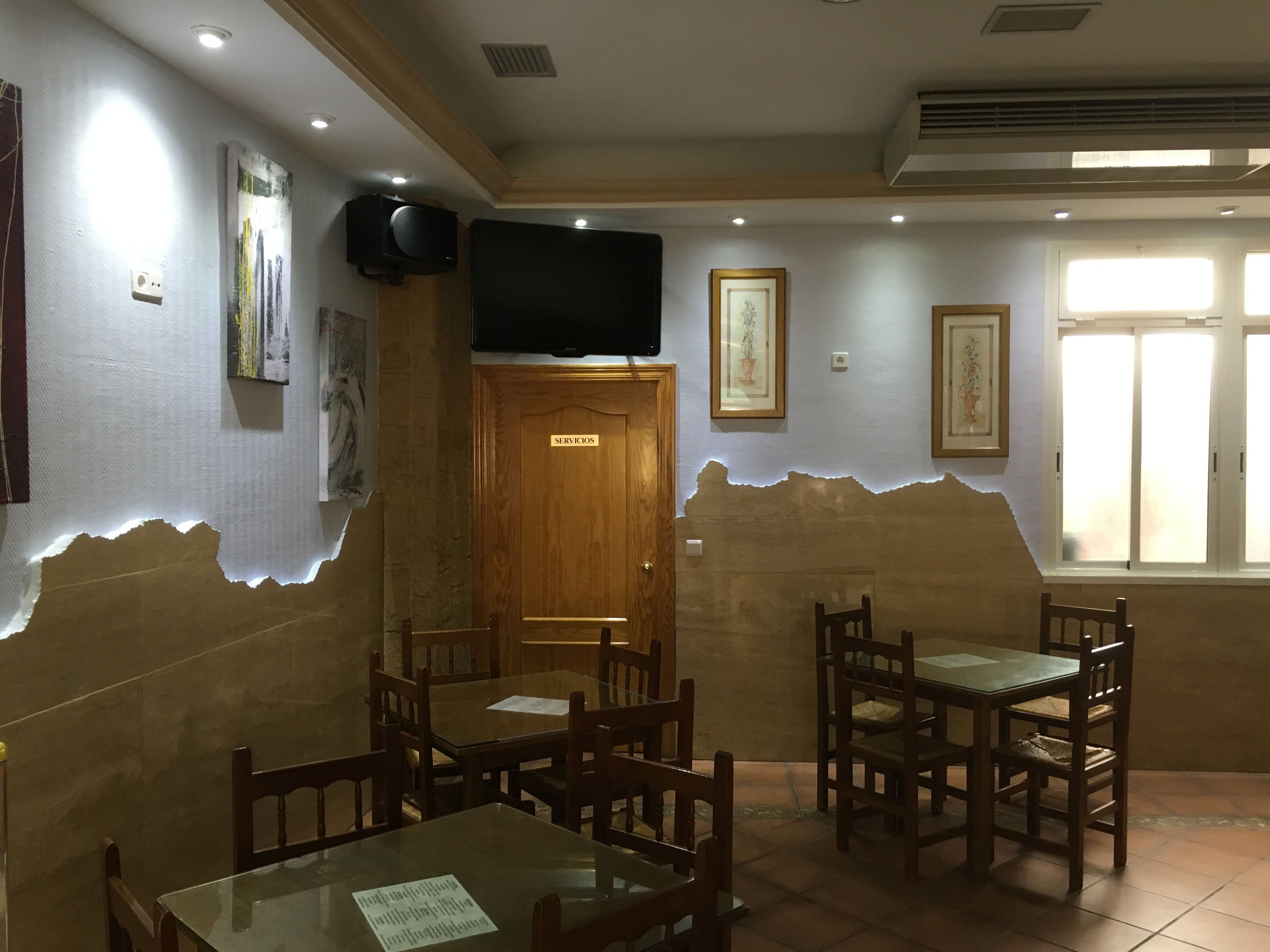 Restaurante com mesas e cadeiras de madeira, uma televisão na parede e obras de arte emolduradas nas paredes.