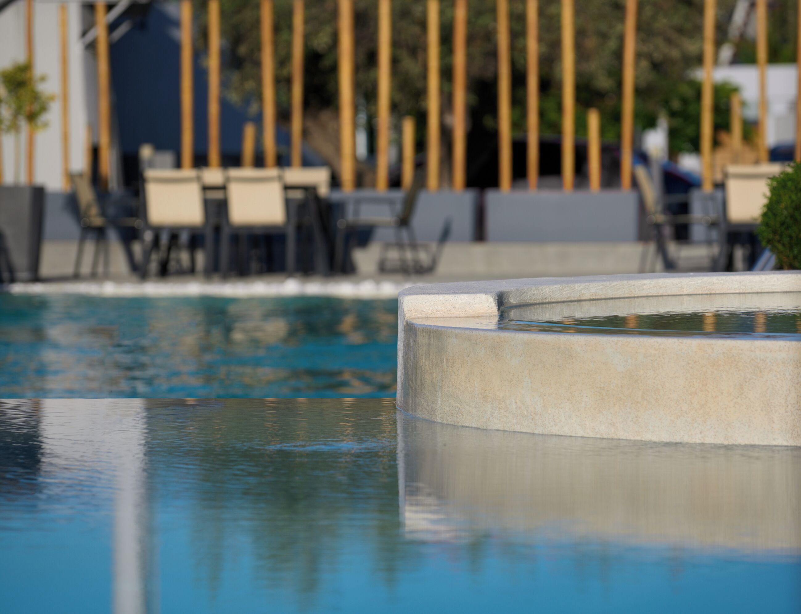 Piscina com borda de concreto, rodeada por cadeiras de sol e um edifício ao fundo.