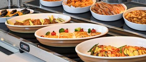 Buffet com diversos pratos, incluindo frutos do mar, legumes e carnes.