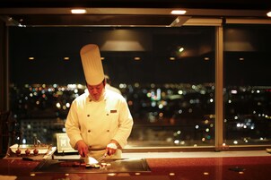 Um chef preparando comida no balcão, com vista para a cidade ao fundo.