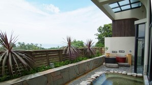 Uma área moderna de piscina externa com degraus de pedra que levam à água, cercada por um muro de madeira e plantas tropicais.