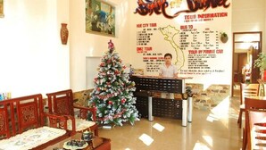 Um saguão com balcão de recepção, uma árvore de Natal e um painel com informações sobre passeios.