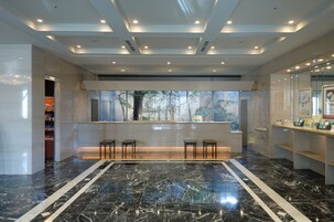 Um hall moderno com piso de mármore, balcão de recepção e vista para árvores através de grandes janelas.