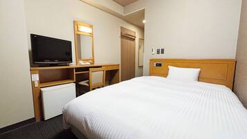 Quarto de hotel com cama, escrivaninha com televisão, espelho e pequeno frigorífico.