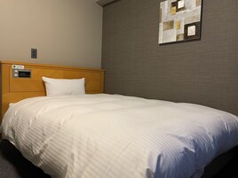 Quarto de hotel com cabeceira de madeira, colcha branca e uma obra de arte pendurada na parede.