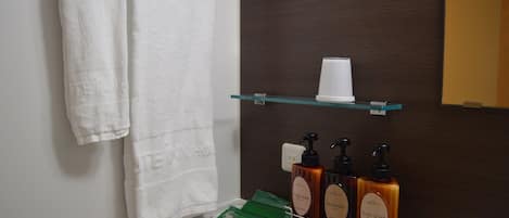 Um banheiro com uma toalha branca pendurada na parede, uma prateleira de vidro com uma xícara e três frascos de sabonete líquido.