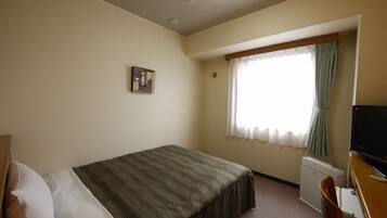 Quarto de hotel com uma cama, uma escrivaninha com computador, janela com cortinas e um pequeno aquecedor.