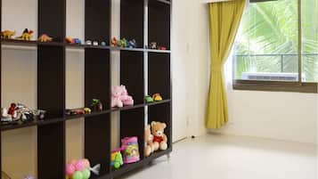 Quarto com uma estante preta cheia de brinquedos e uma janela com cortinas amarelas.