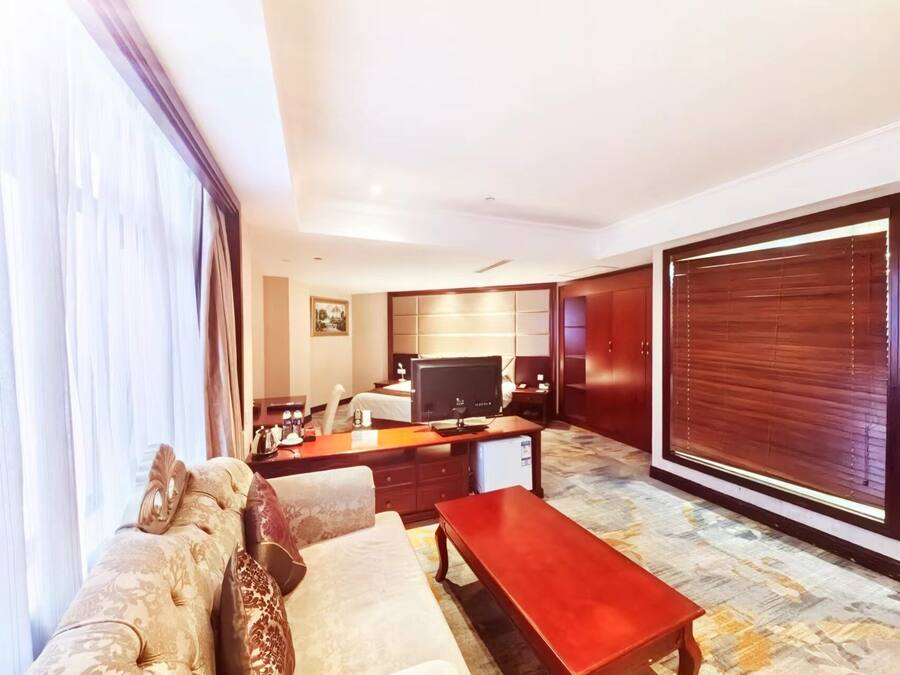 Quarto de hotel com sofá, mesa de centro de madeira, escrivaninha com computador, televisão e guarda-roupa.