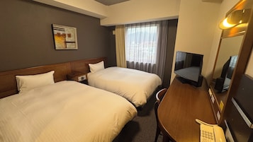 Quarto de hotel com duas camas, uma escrivaninha com telefone, televisão e uma janela com cortinas.