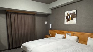 Quarto de hotel com uma cama grande, uma mesinha de cabeceira, uma luminária, um quadro na parede e uma janela com cortinas.