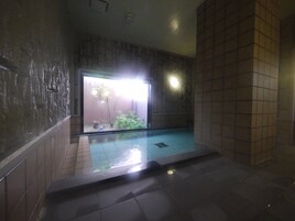 Uma área de piscina interior com pouca luz, paredes azulejadas e um elemento aquático visível.