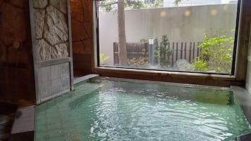 Área de spa com parede de pedra, janela com vista para cerca e vegetação, e uma pequena piscina.