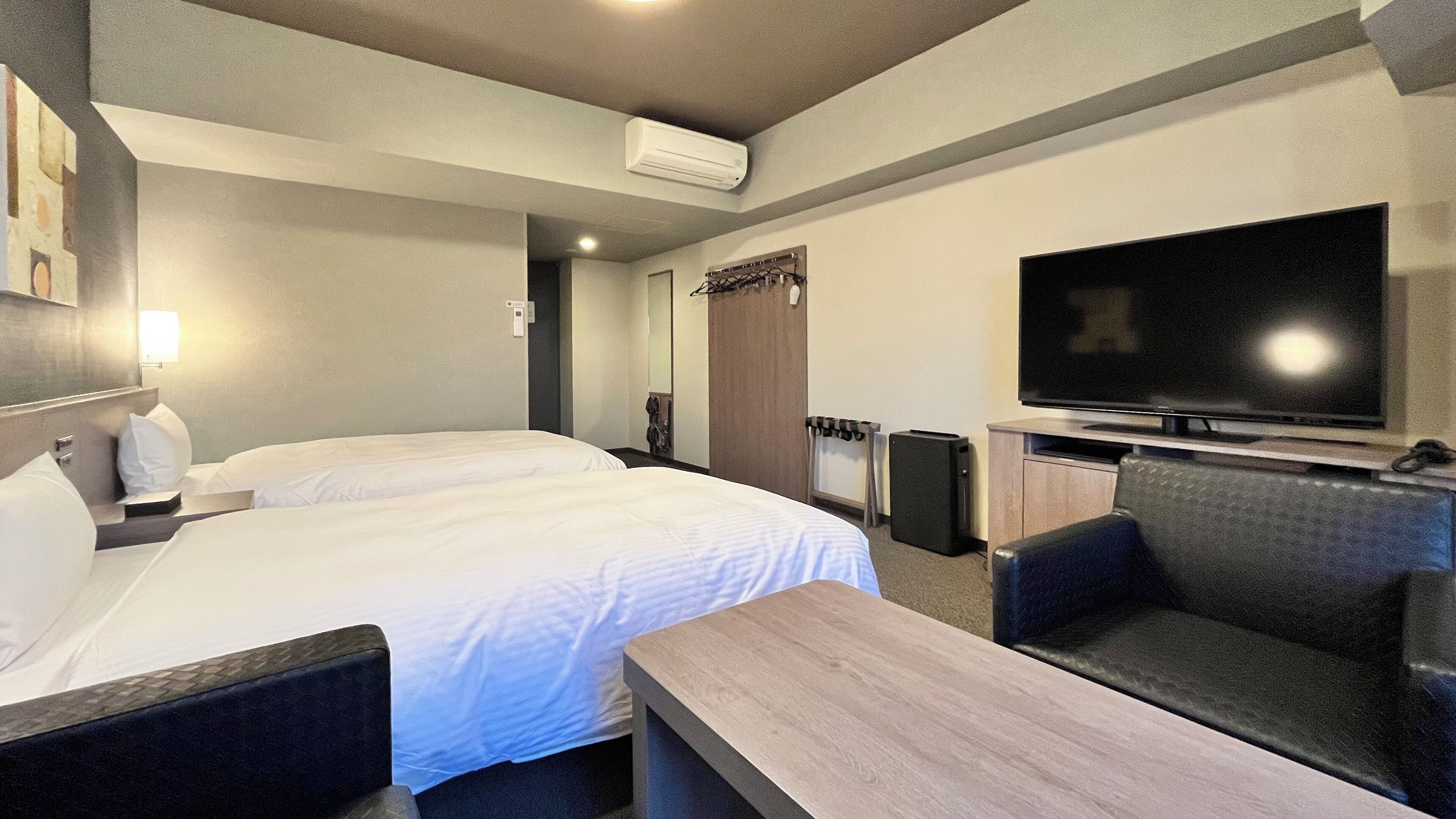 Quarto de hotel com duas camas, uma televisão, uma escrivaninha e uma cadeira.
