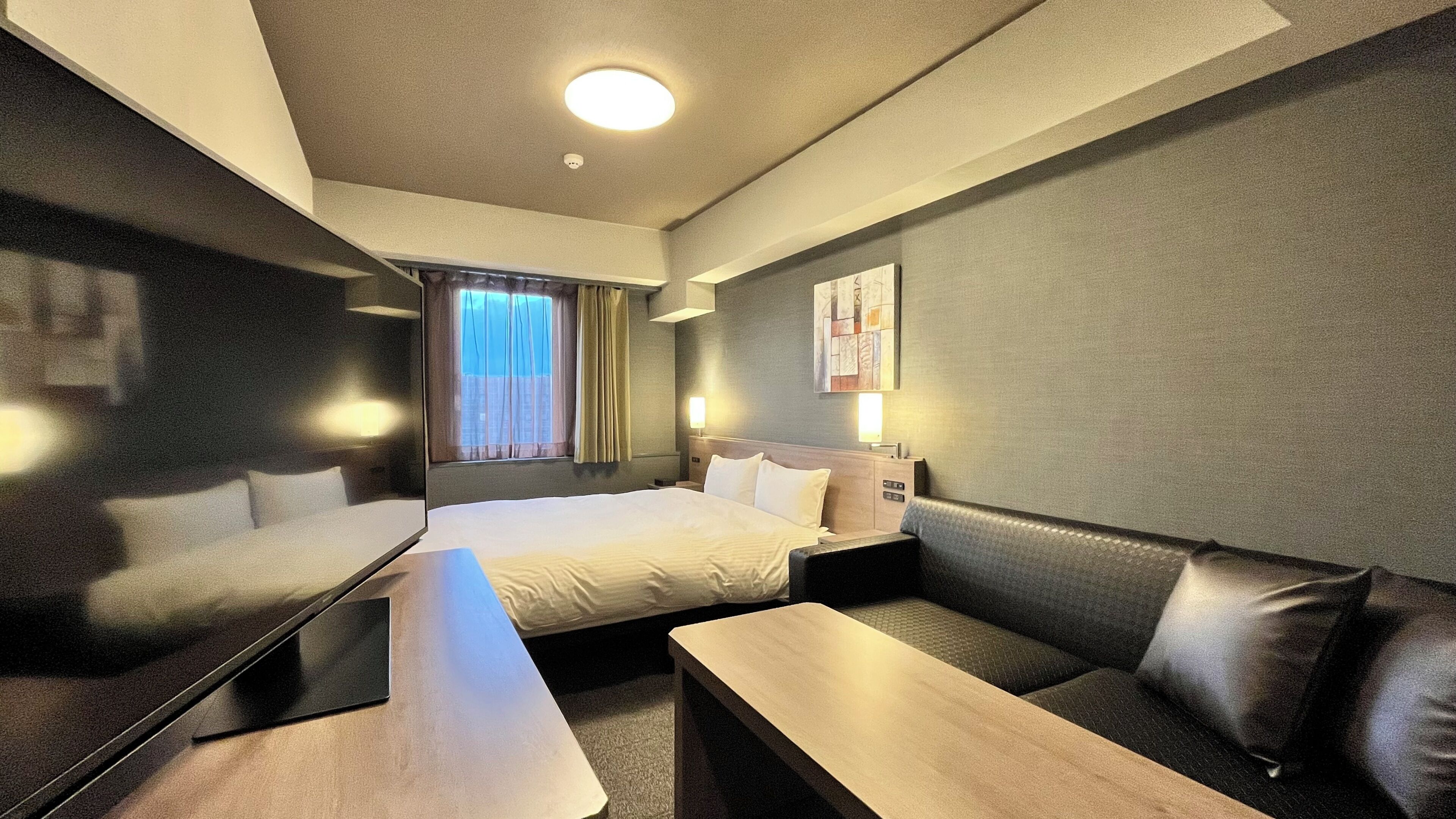 Quarto de hotel com cama, sofá, mesa e janela com cortinas.