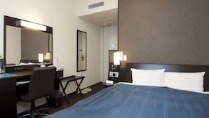 Quarto de hotel com cama, escrivaninha, cadeira e um espelho grande.