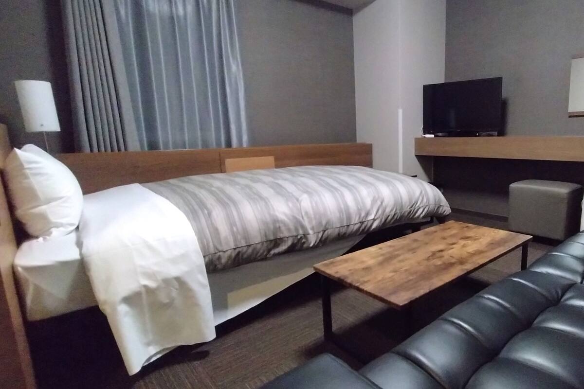 Quarto de hotel com cama, mesa de madeira, sofá de couro, televisão e escrivaninha.