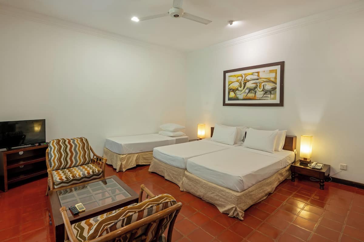 Quarto de hotel com cama, duas mesas de cabeceira com luminárias, televisão, sofá e poltrona.