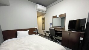 Quarto de hotel com uma cama grande, uma escrivaninha com cadeira, televisão e ar condicionado.