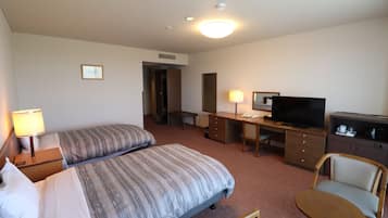 Quarto de hotel com duas camas, uma escrivaninha, uma cadeira, uma televisão e uma luminária.