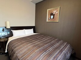 Quarto de hotel com cama, mesa de cabeceira, abajur e uma obra de arte na parede.