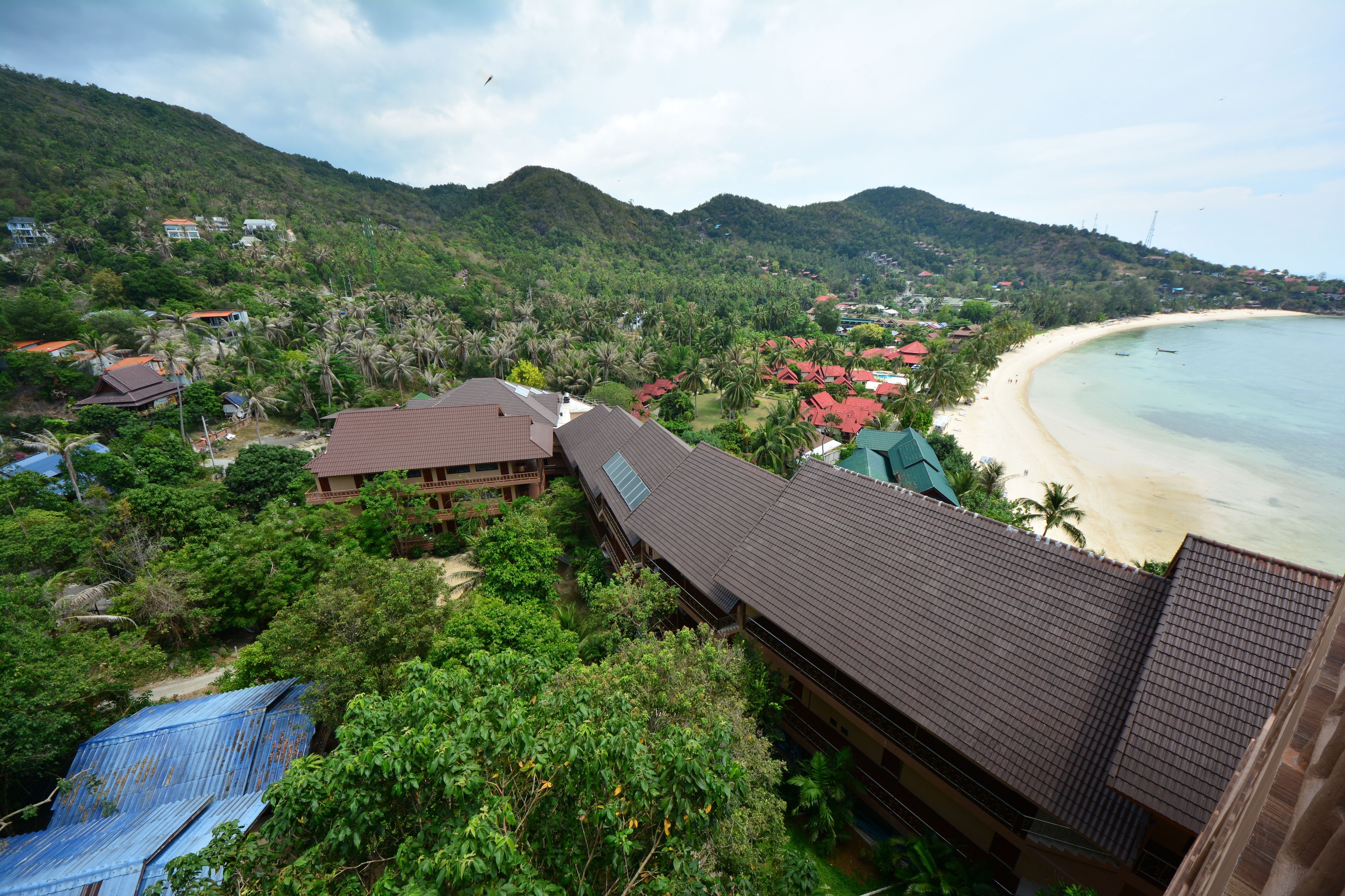 Um resort costeiro com vista para a praia, rodeado por vegetação exuberante e colinas.