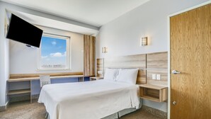 Quarto de hotel moderno com cama, escrivaninha, cadeira, televisão e guarda-roupa.