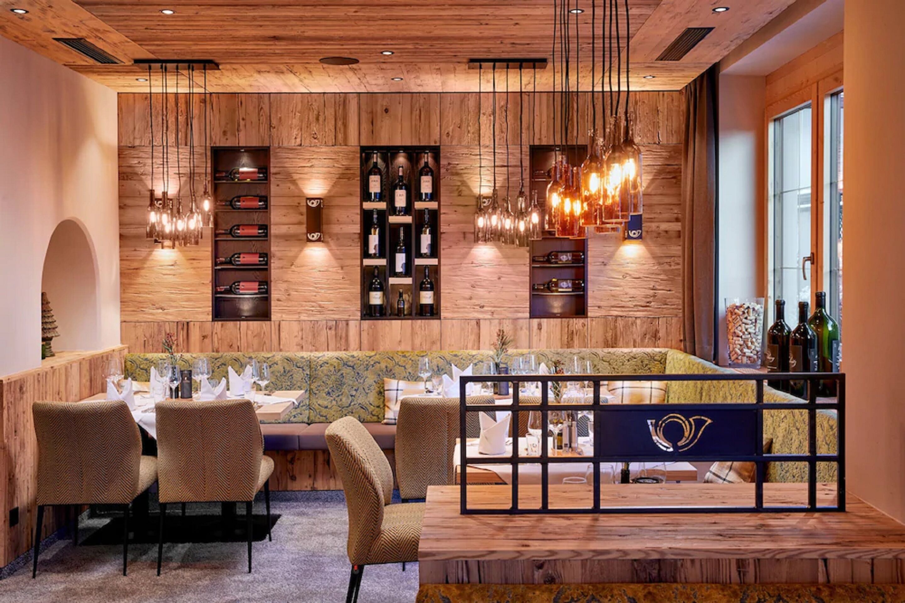 Um restaurante com decoração em madeira, área de bar com garrafas e disposição de mesas e cadeiras.