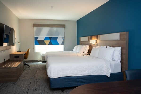 Quarto de hotel com uma cama grande, uma escrivaninha, uma cadeira, uma televisão e uma janela com vista geométrica.