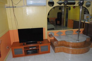 Quarto com televisão de tela plana em suporte de madeira, um espelho e uma pequena mesa com abajur.