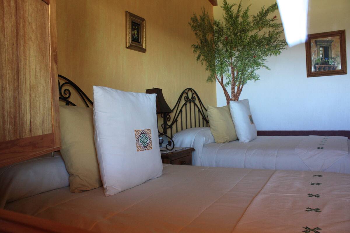 Quarto de hotel com duas camas, um guarda-roupa de madeira, um vaso de planta e um quadro na parede.