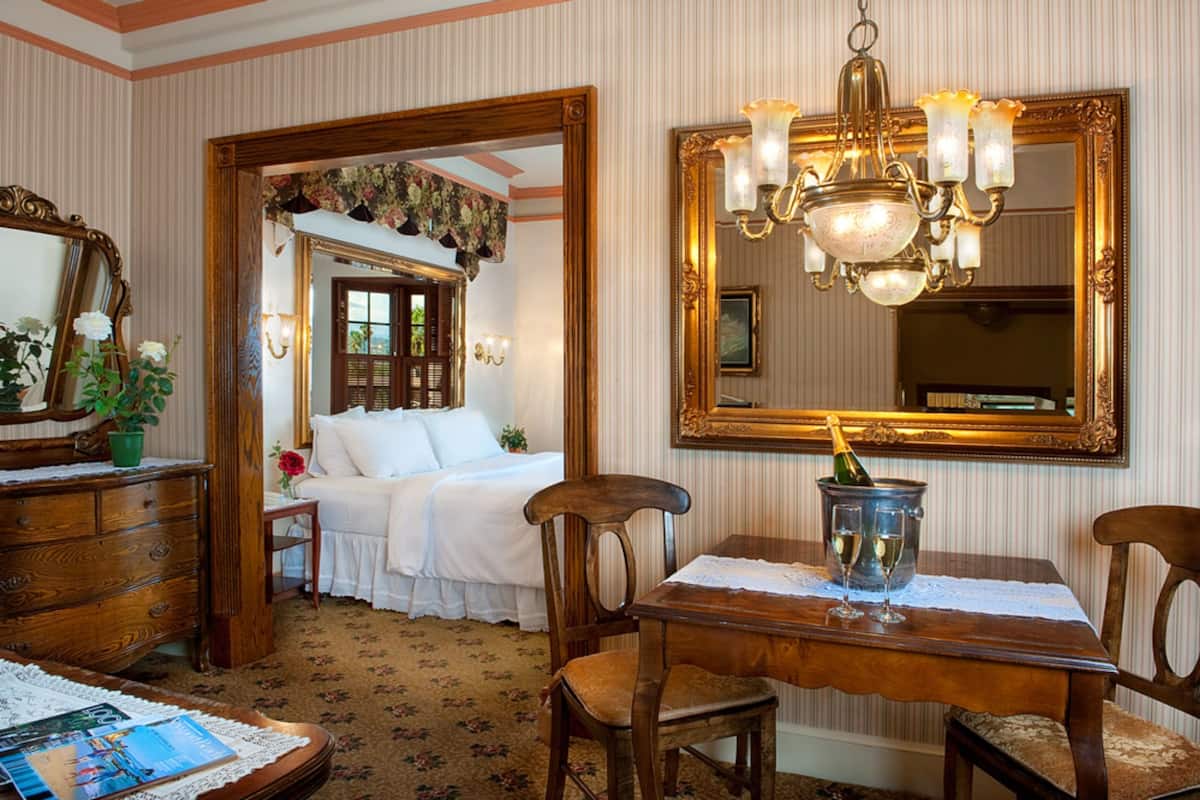 Um quarto com uma mesa de jantar de madeira, um candelabro, um espelho grande e uma cama com roupa de cama branca.