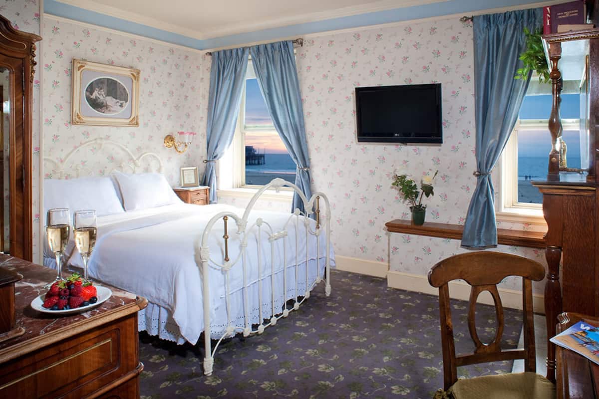 Quarto com cama, escrivaninha, cadeira, televisão e vista para o mar.