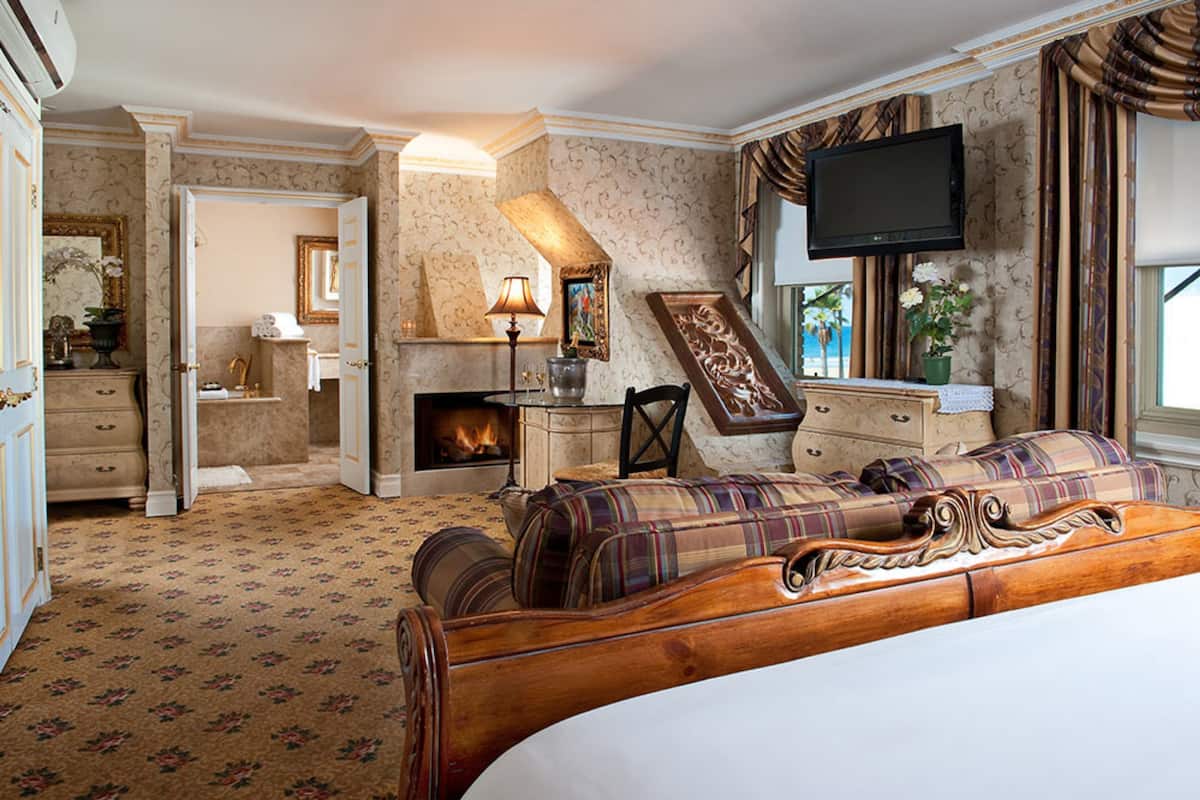 Quarto de hotel com cama, lareira, televisão e banheiro visível por uma porta aberta.