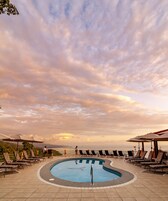 Área de piscina com espreguiçadeiras e guarda-sóis, cercada por um deck revestido de azulejos.