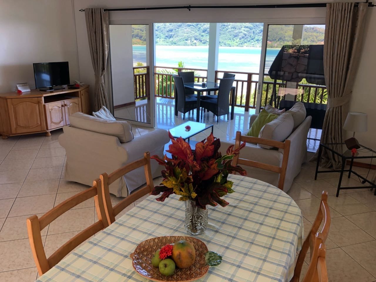 Uma área de refeições com uma mesa posta para dois, uma televisão e vista para o mar.
