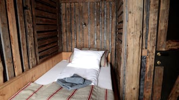 Uma cama pequena com estrutura de madeira, roupa de cama branca e manta listrada.