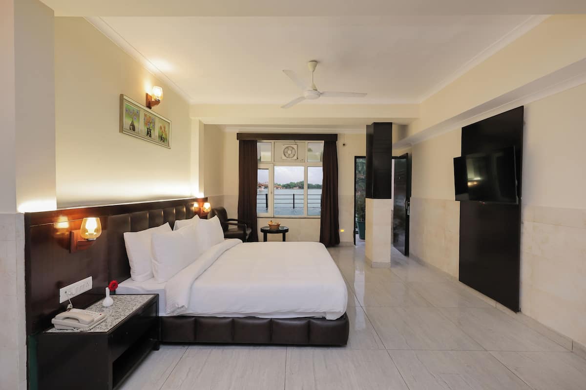 Quarto de hotel com cama grande, mesa de cabeceira com abajur, ventilador de teto, televisão e janela com vista.
