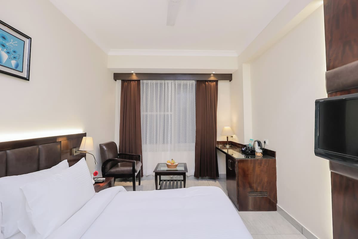 Quarto de hotel com cama, escrivaninha, cadeira, televisão e janela com cortinas.