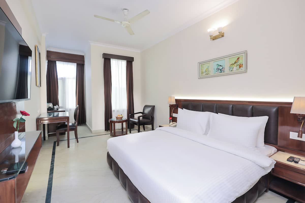 Quarto de hotel com uma cama grande, uma escrivaninha com cadeira, televisão e um quadro na parede.