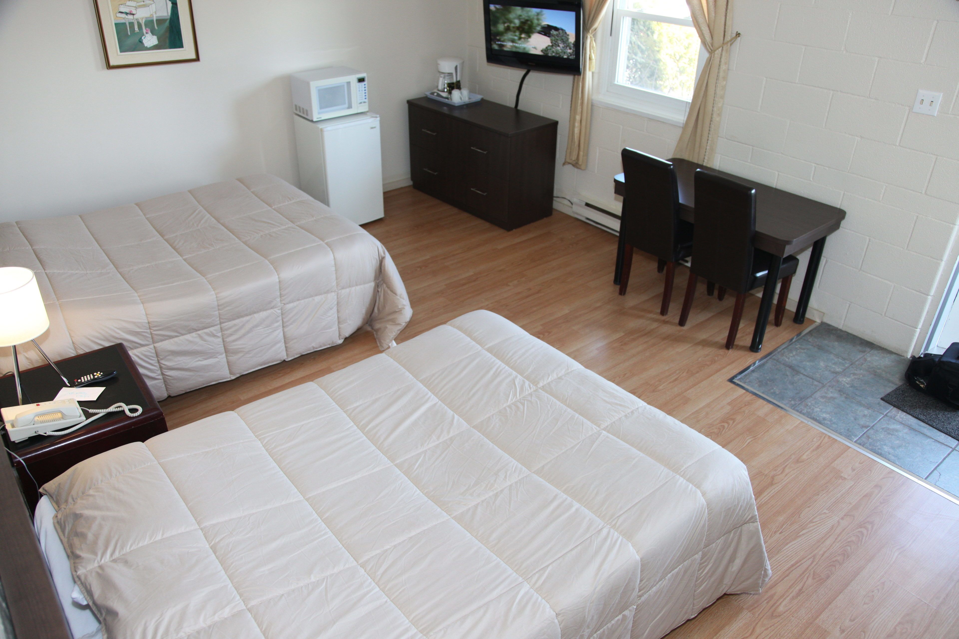 Quarto de hotel com duas camas, uma escrivaninha, televisão e uma pequena cozinha.