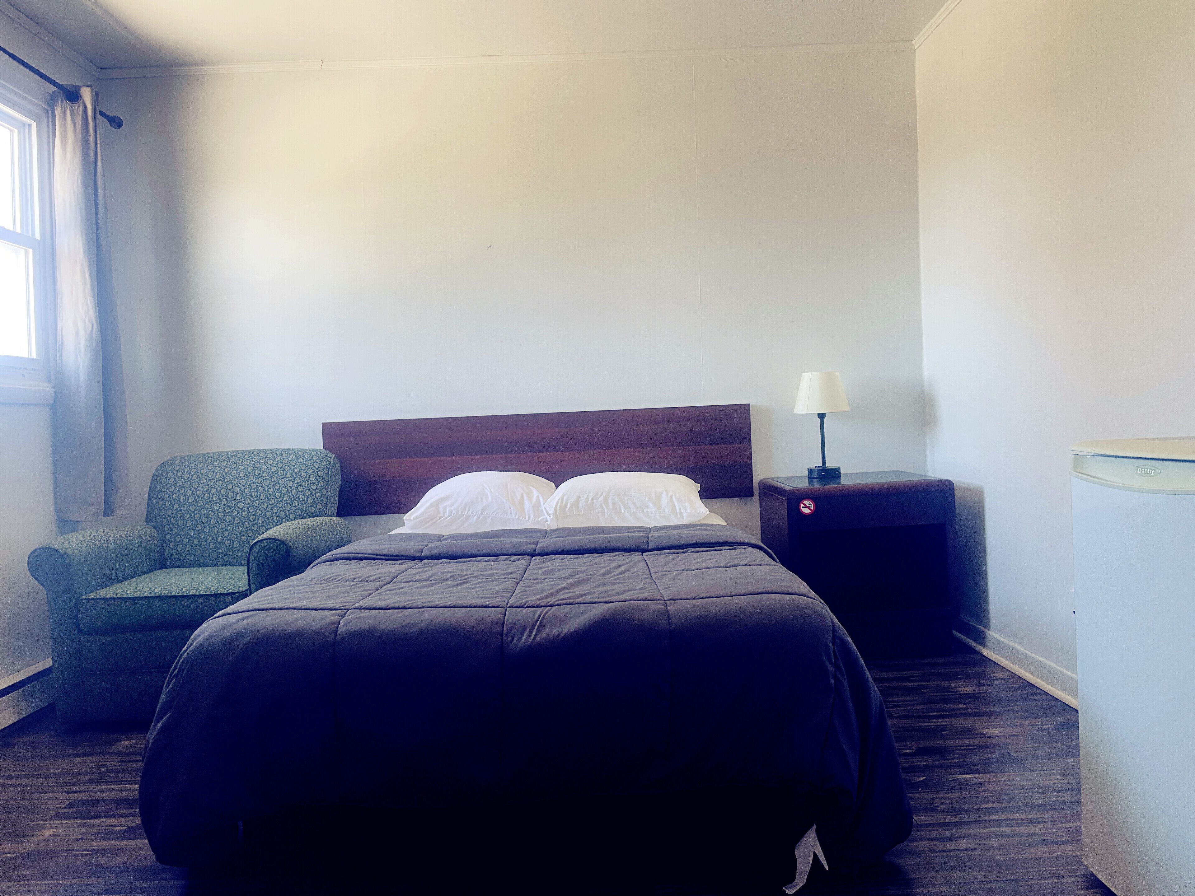 Quarto de hotel com cama, uma cadeira, mesa de cabeceira e abajur.