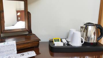 Quarto de hotel com mesa de cabeceira de madeira, espelho, bandeja com chaleira, chávenas e comando remoto.