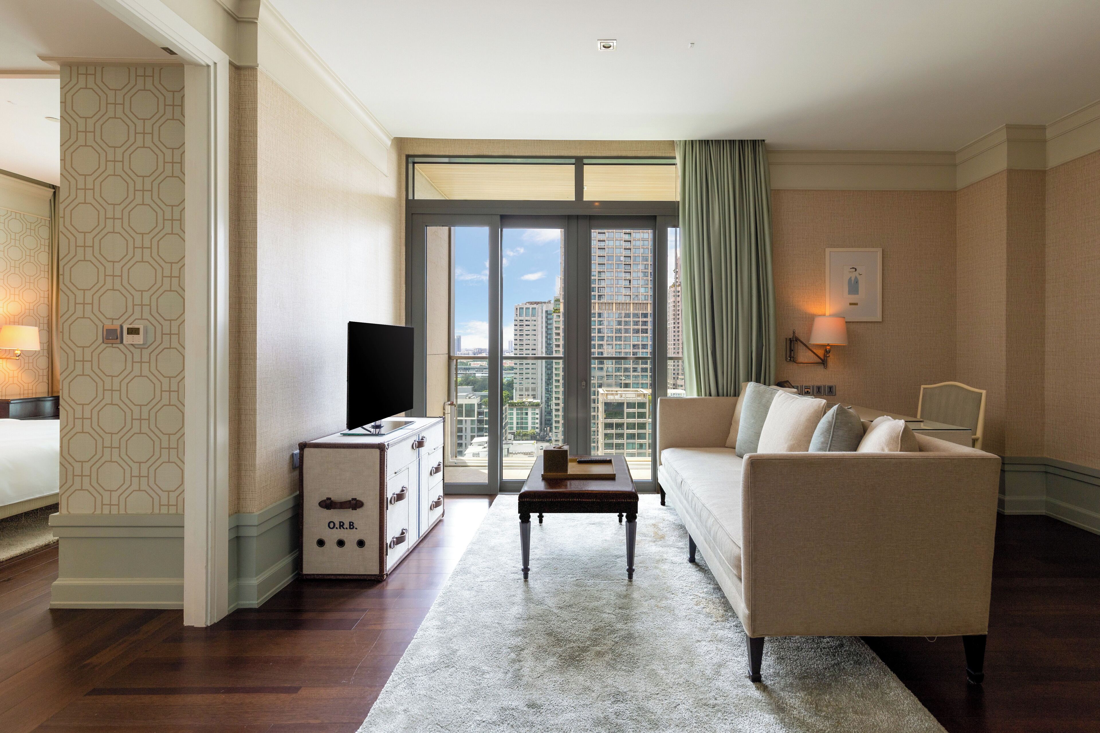 Quarto de hotel moderno com uma janela grande, um sofá, uma mesa de centro e uma TV em uma cômoda.