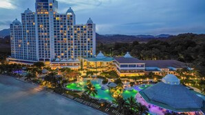 Um grande hotel com várias torres, um pátio central com piscina e áreas ajardinadas ao redor.