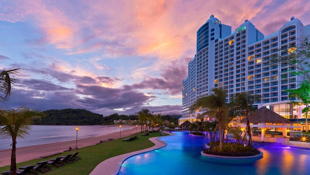 Um hotel com piscina, praia e palmeiras.