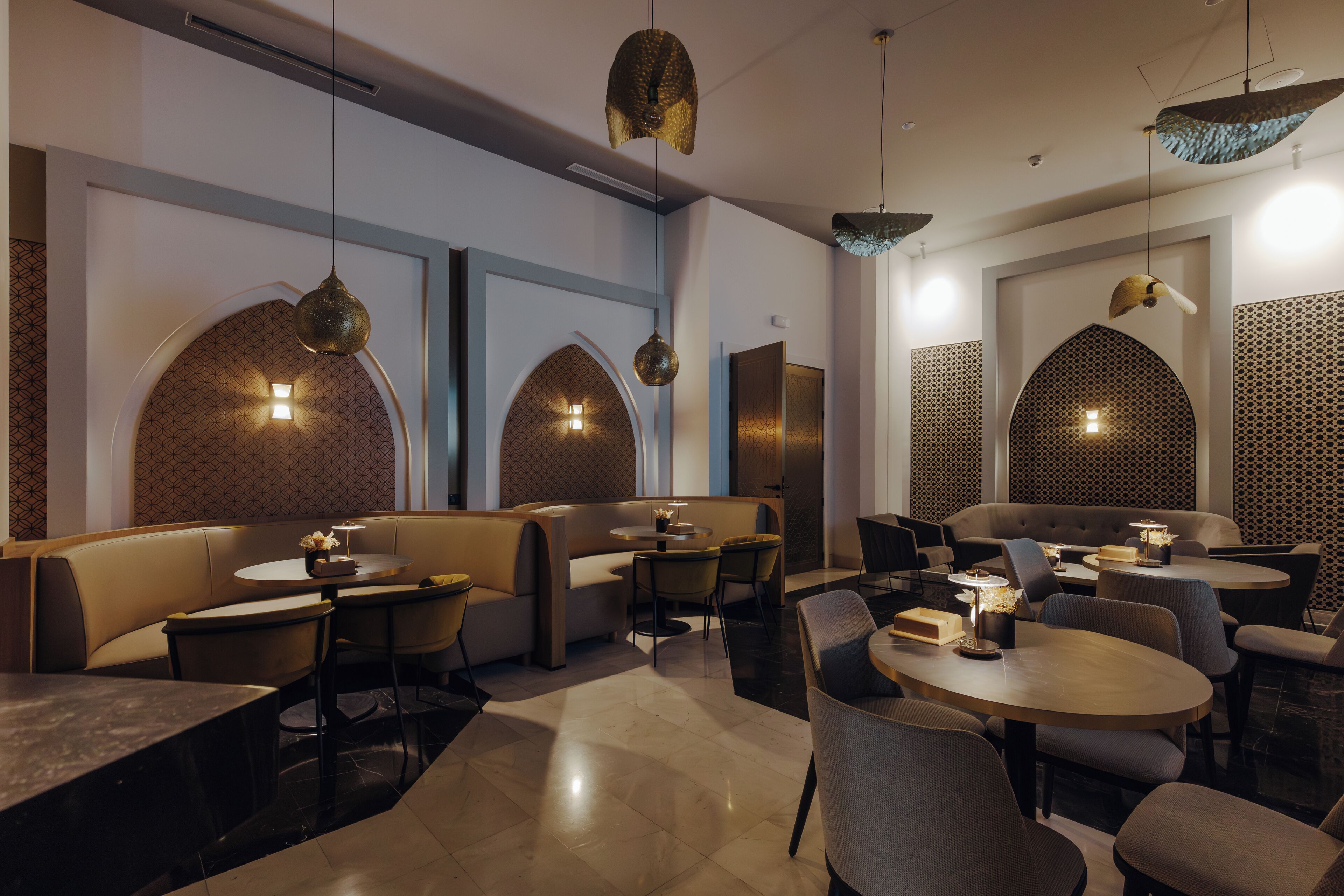 Interior moderno de restaurante com cabines, mesas redondas e luminárias pendentes.