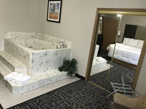 Um banheiro moderno com uma banheira de pedestal, um espelho grande e uma cama bem arrumada.